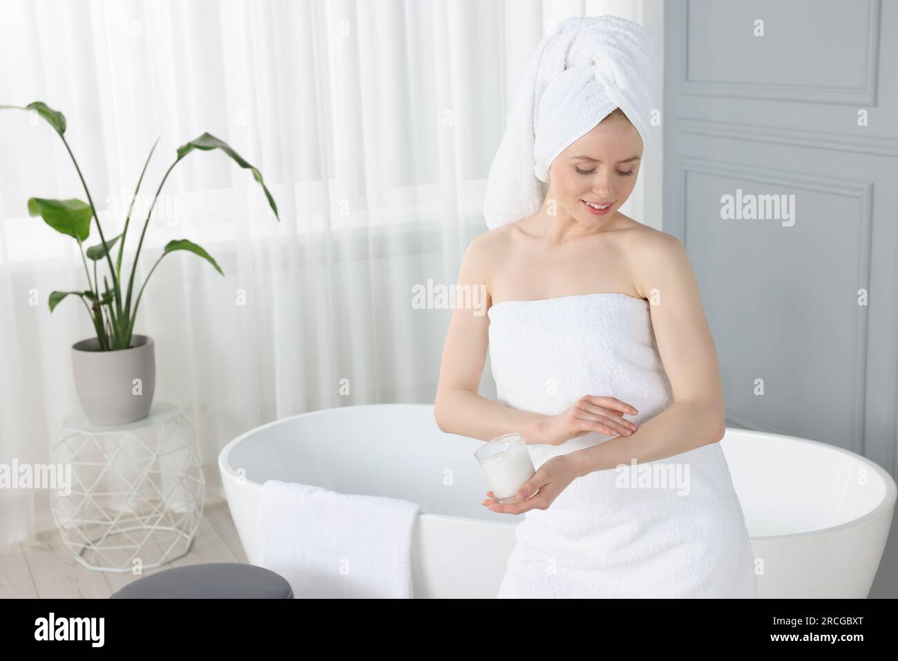Beautiful young woman applying body cream onto arm in bathroom Stock ...