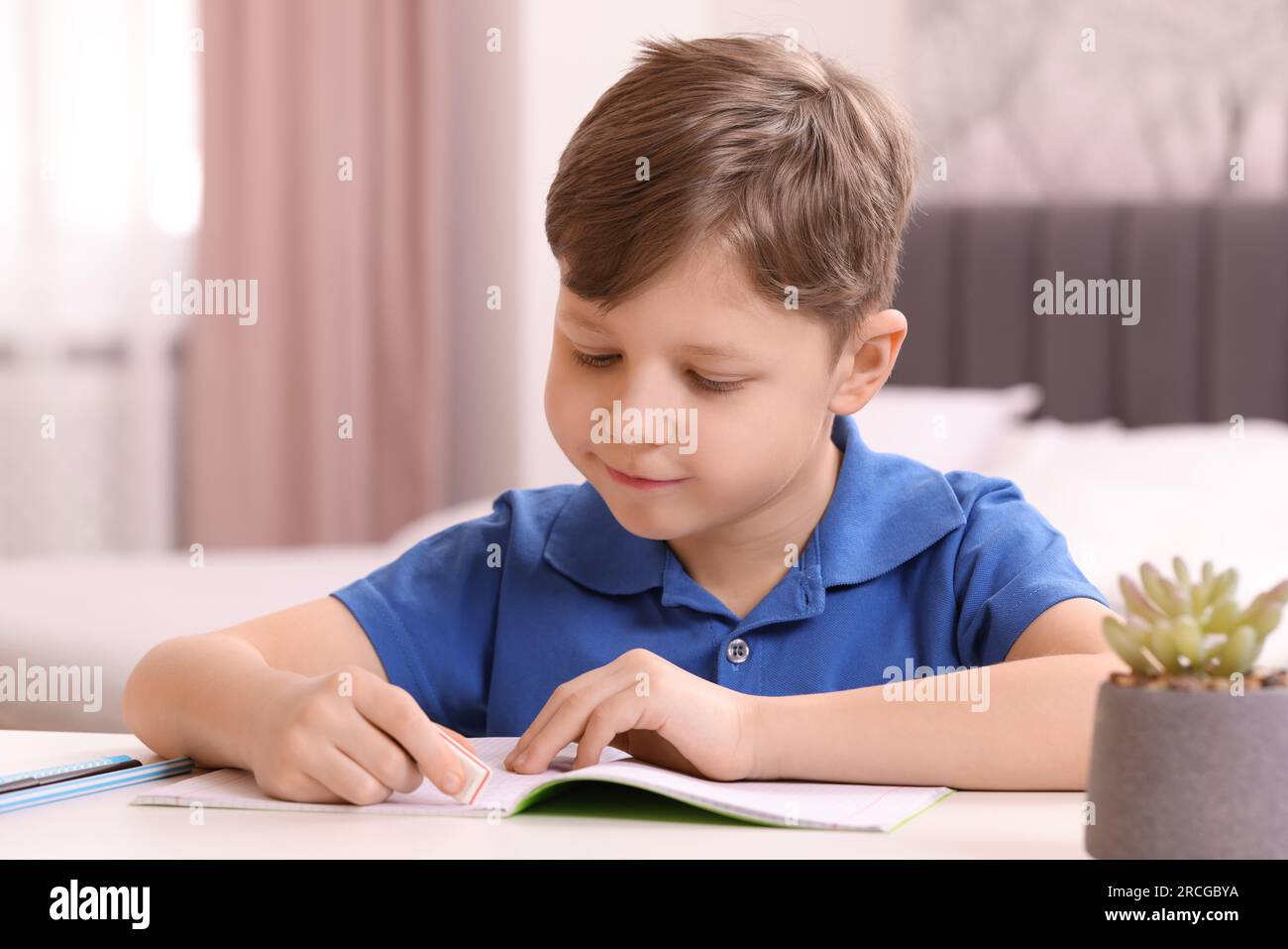 Little boy erasing mistake in his notebook at white desk indoors Stock ...