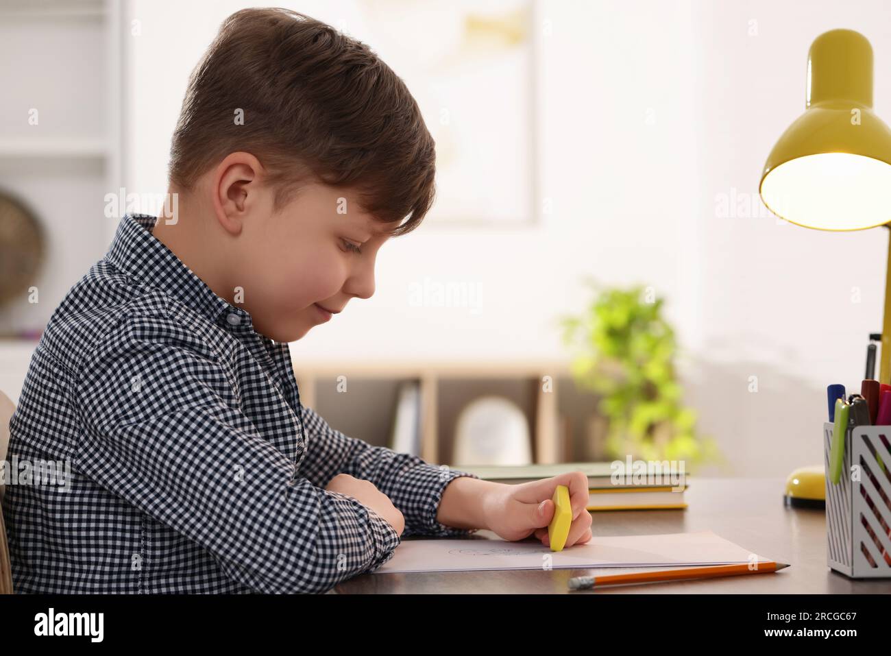 Little boy erasing mistake in his notebook at wooden desk indoors Stock ...