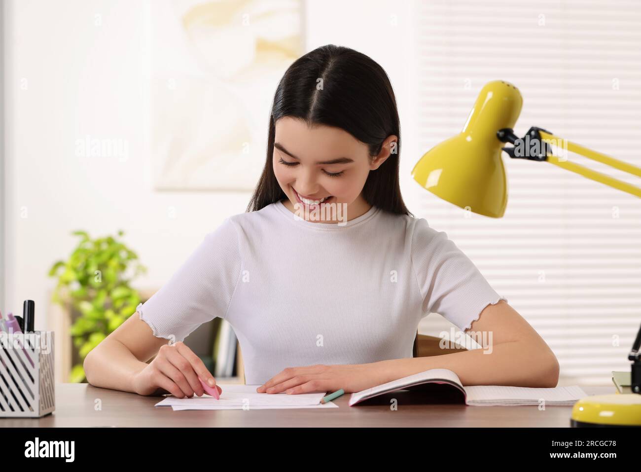 Teenage girl erasing mistake in her notebook at wooden desk indoors ...