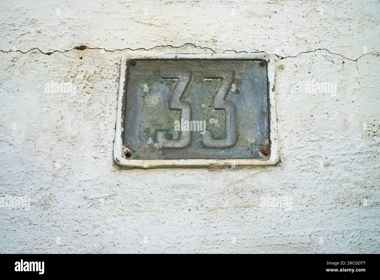 Number 33, thirty-three, old house number plate on a weathered wall ...