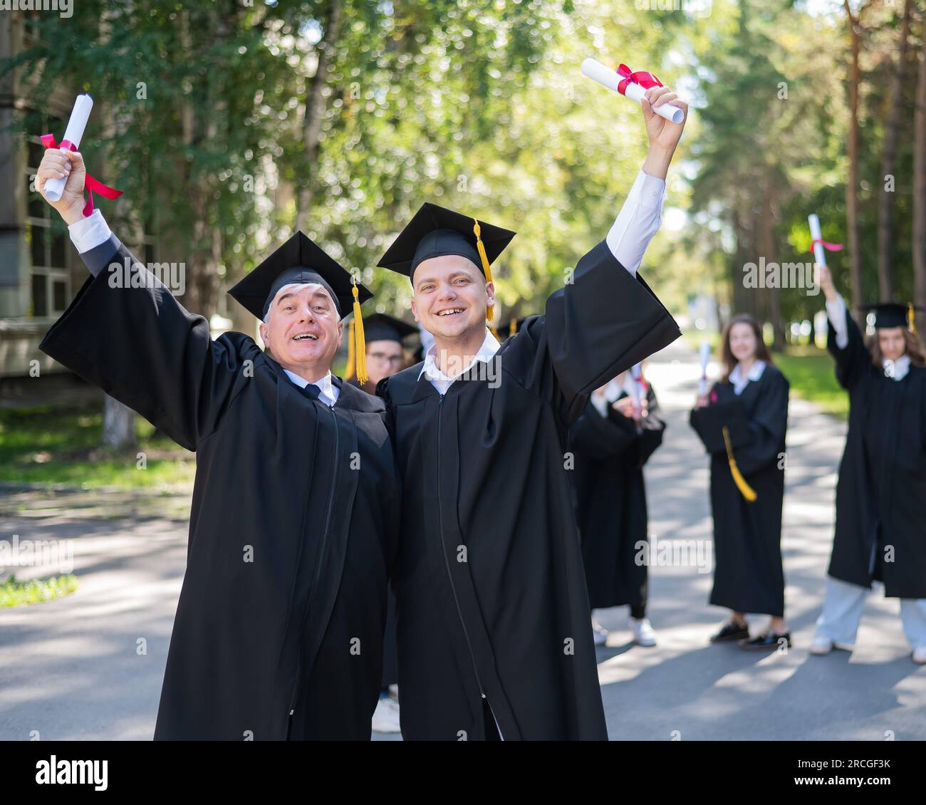 A group of graduates in robes outdoors. An elderly man and a young guy ...