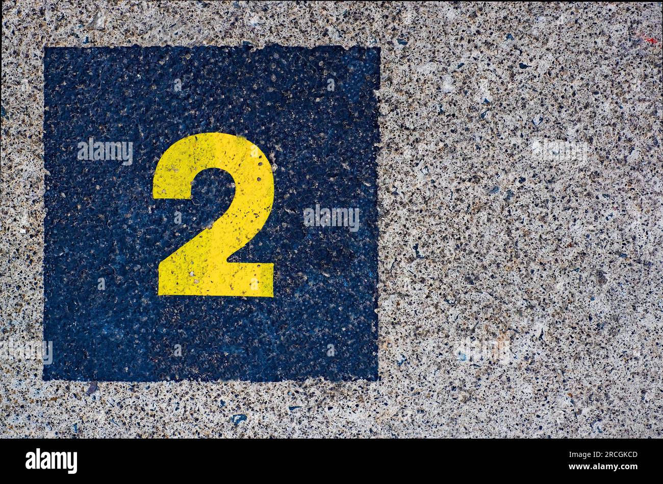 Yellow number 2, two, in dark blue square, offset on flat concrete ...