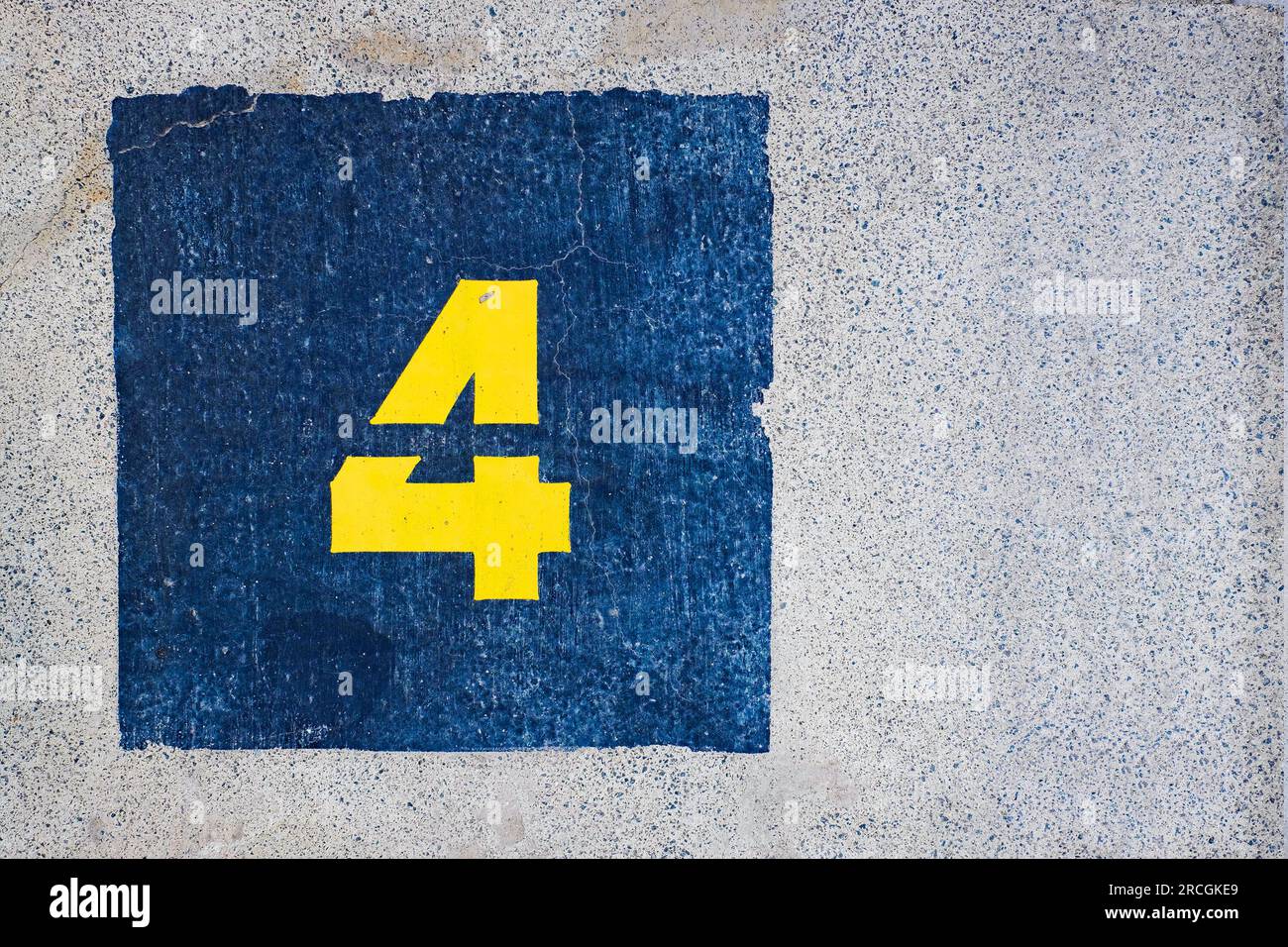 Yellow number 4, four, in dark blue square, offset on flat concrete ...