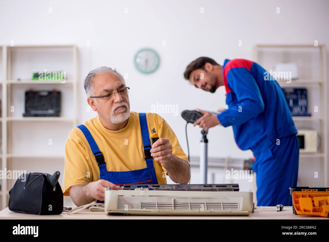 Two repairmen repairing air-conditioner at workshop Stock Photo - Alamy