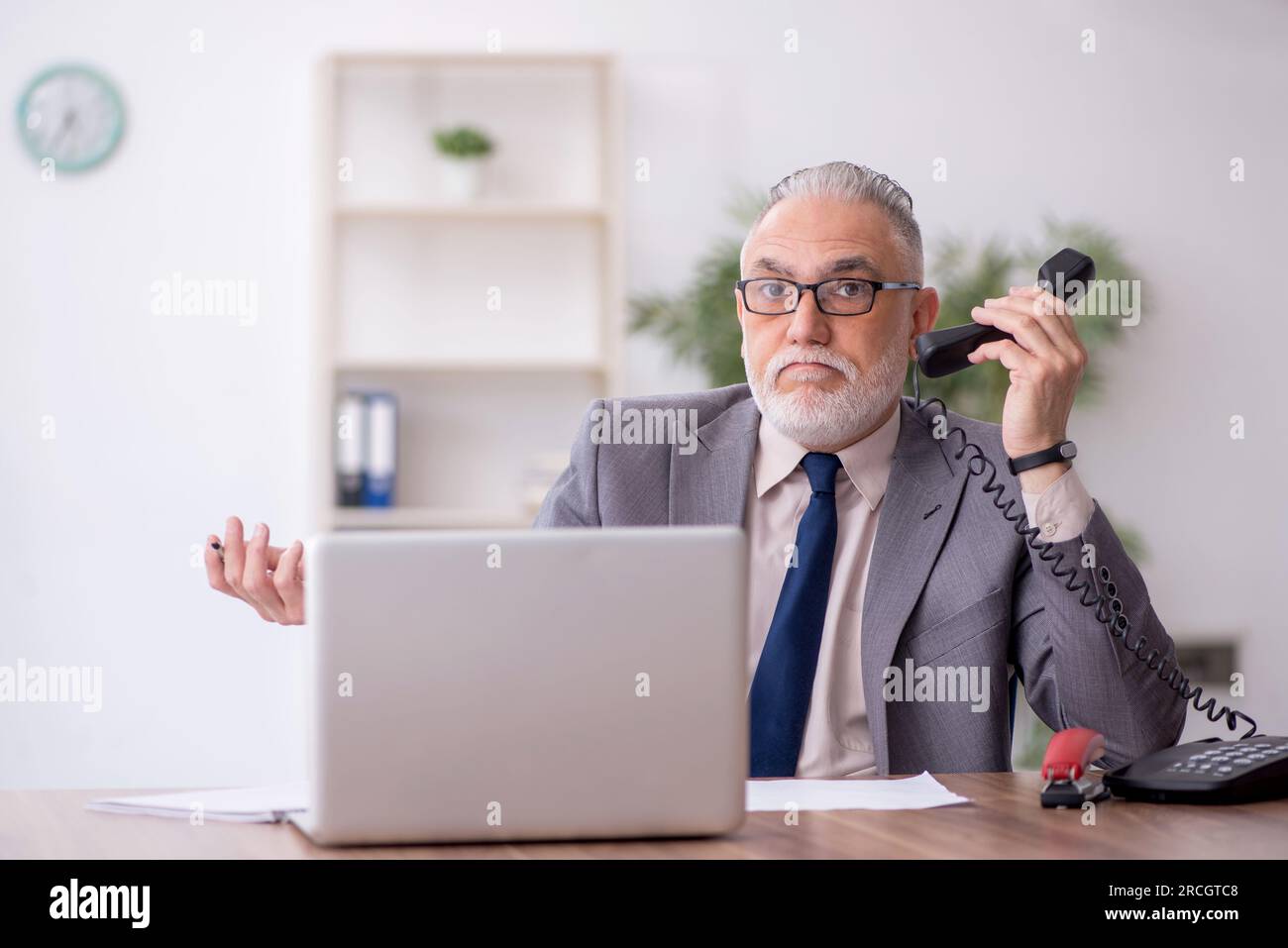 Old employee speaking by phone at workplace Stock Photo - Alamy