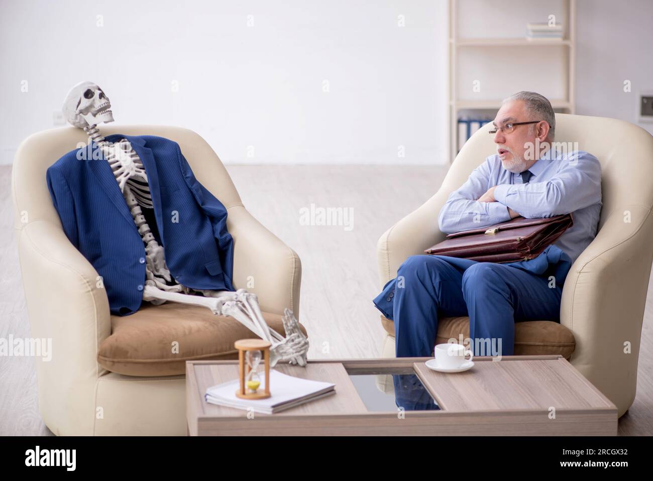 Old male boss and skeleton in business meeting concept Stock Photo - Alamy