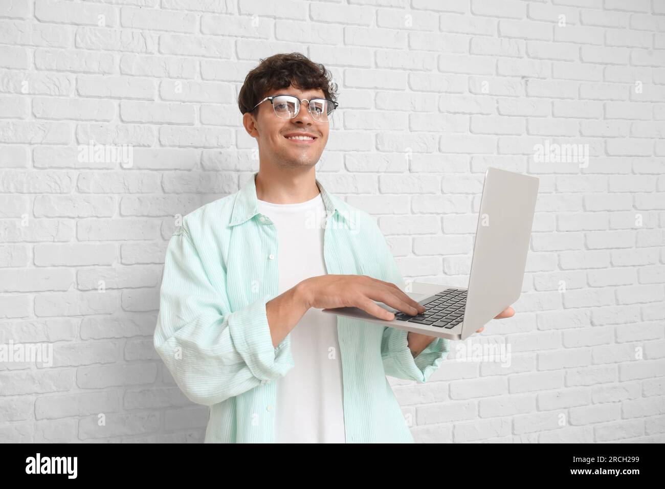 Male programmer working with laptop on white brick background Stock ...