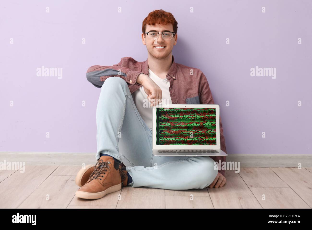 Male programmer with laptop sitting near lilac wall Stock Photo - Alamy