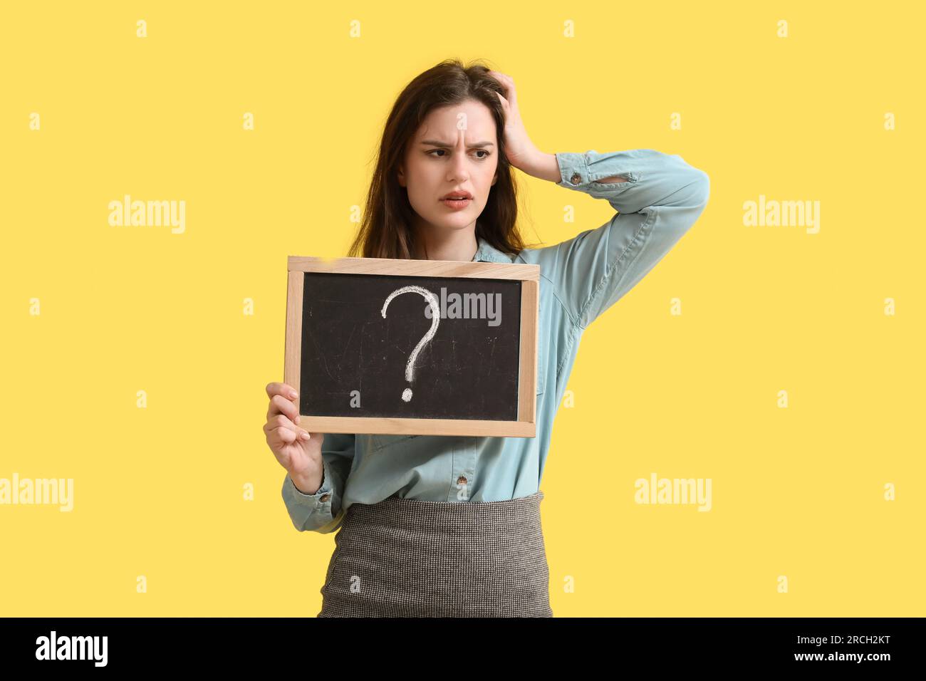 Stressed female teacher holding chalkboard with question mark on yellow ...