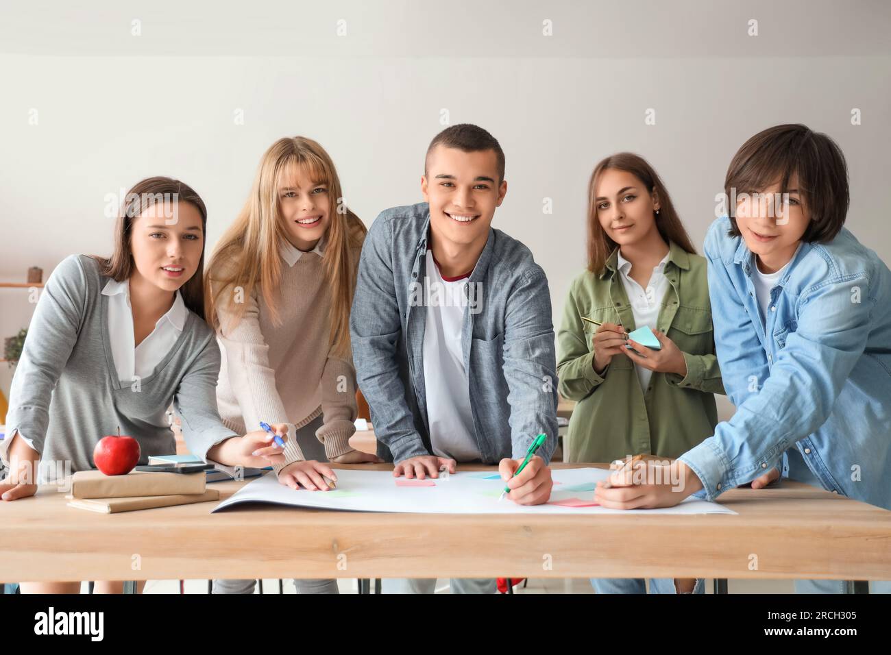 Group of teenage students performing task at table in classroom Stock ...
