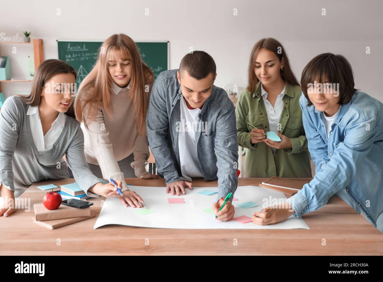 Group of teenage students performing task at table in classroom Stock ...