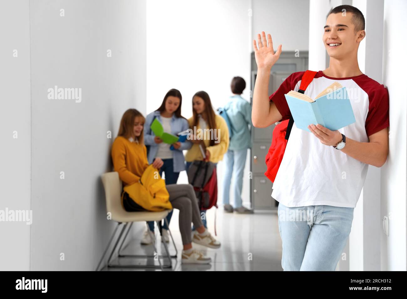 Teenage boy with book waving hand at school Stock Photo - Alamy