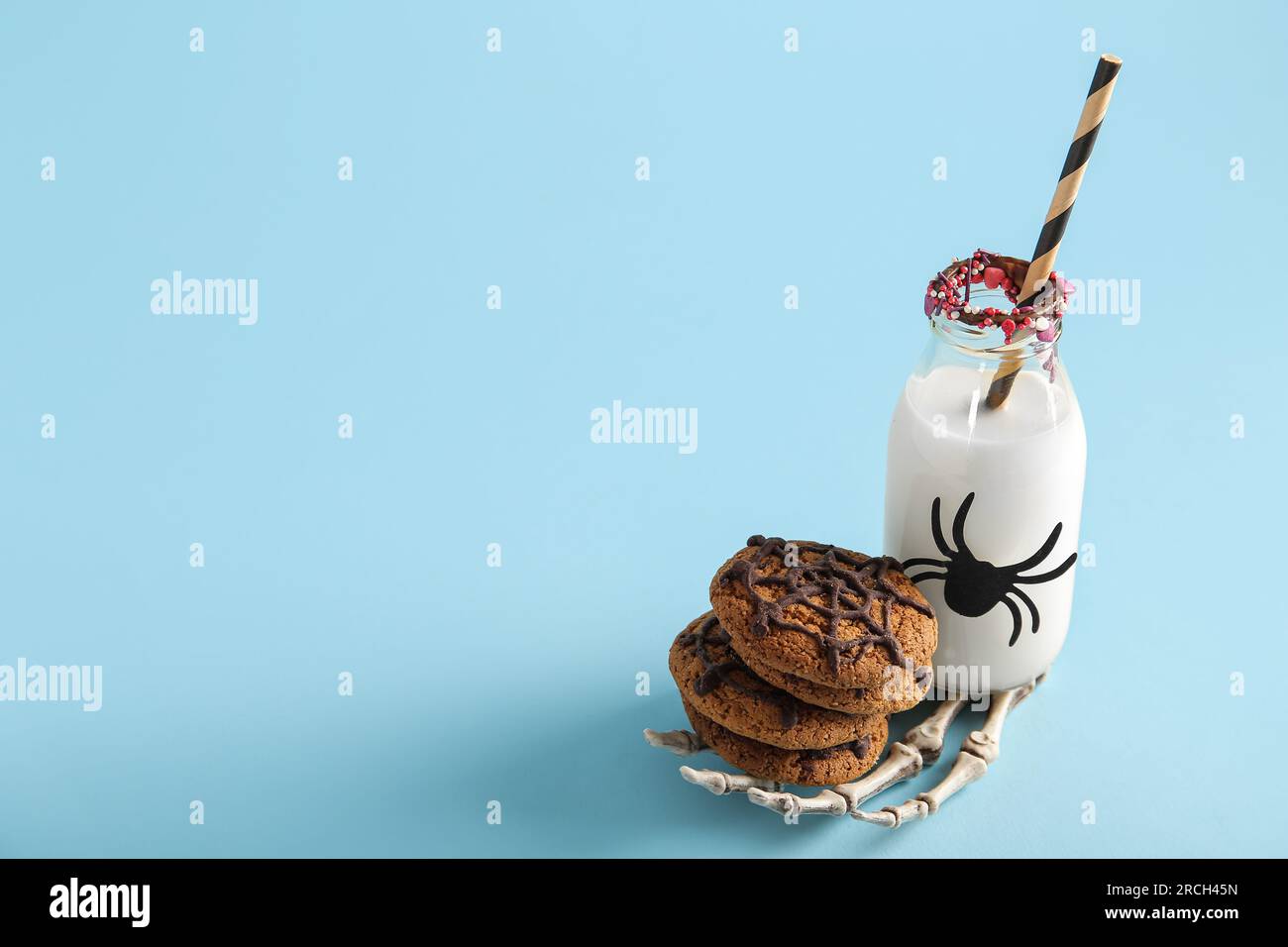 Bottle of milk, skeleton hand and tasty cookies for Halloween on blue ...