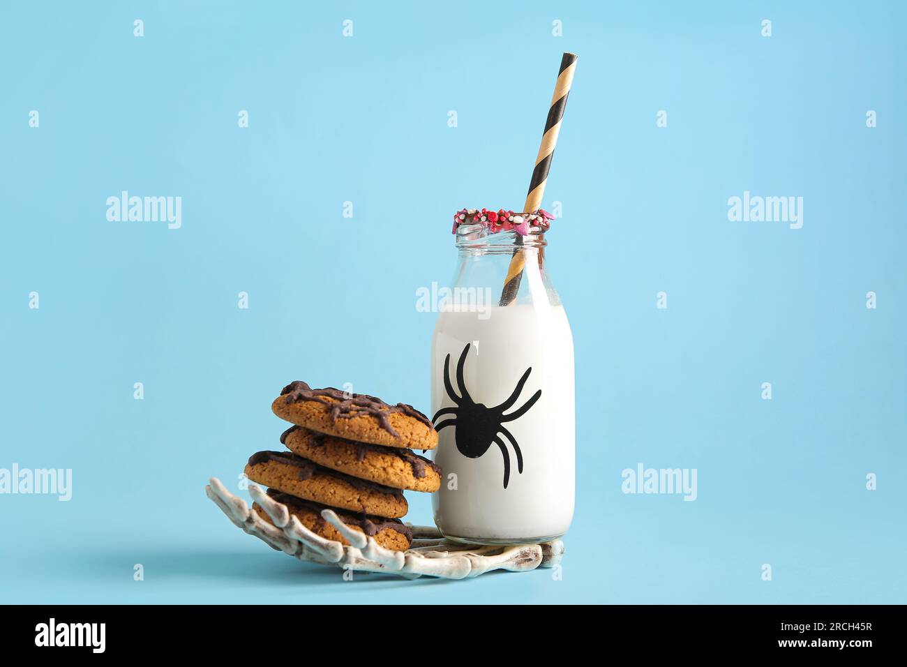 Bottle of milk, skeleton hand and tasty cookies for Halloween on blue ...