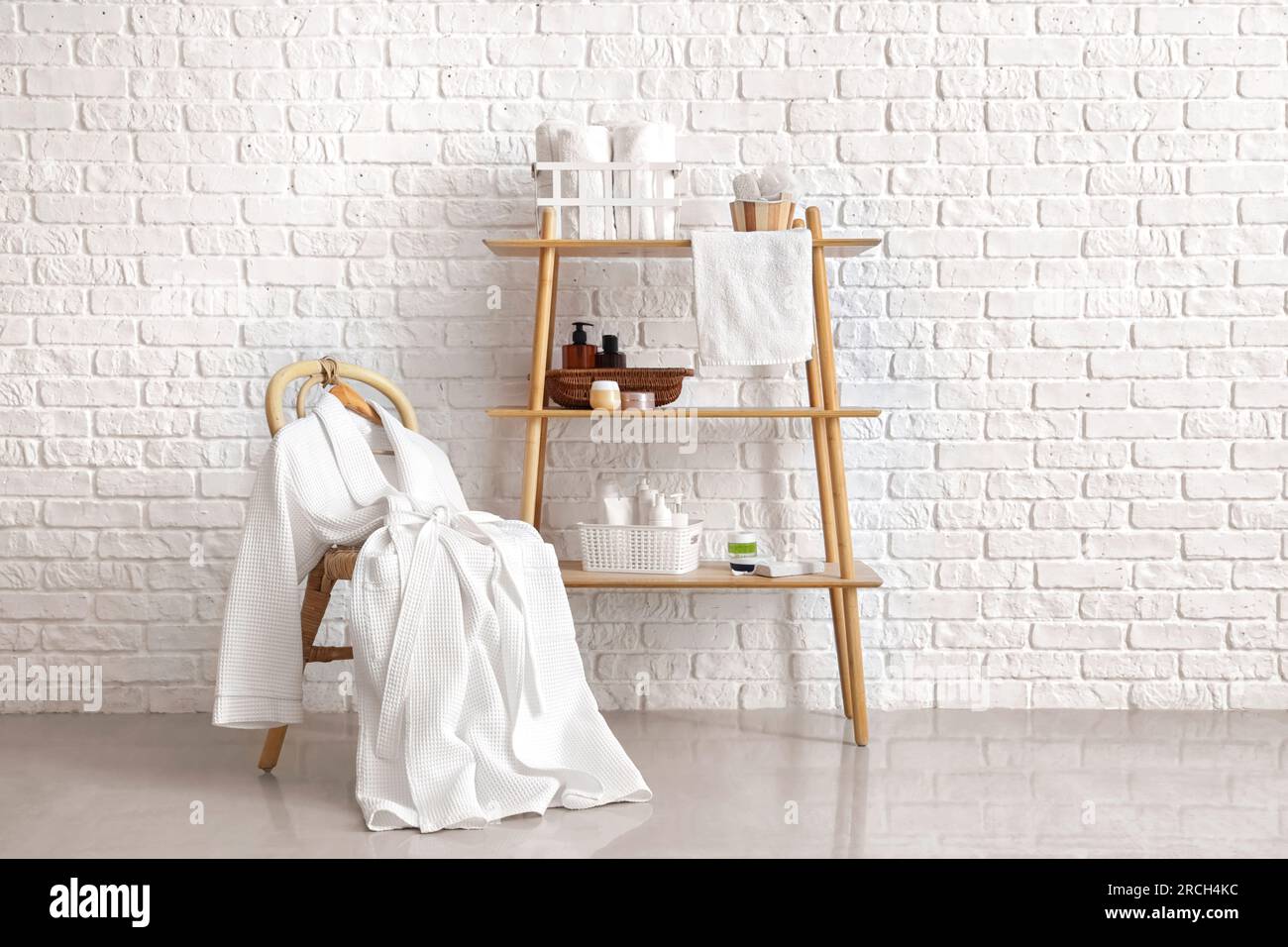 Shelving unit with bath accessories and bathrobe on chair near white ...