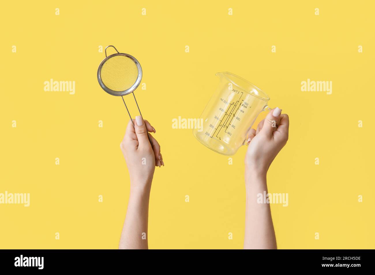 Female hands with sieve and measuring cup on yellow background Stock ...