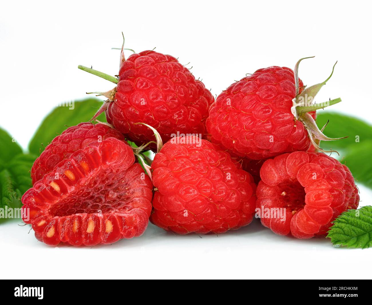 close up of fresh natrual raspberries with halved fruit between green ...