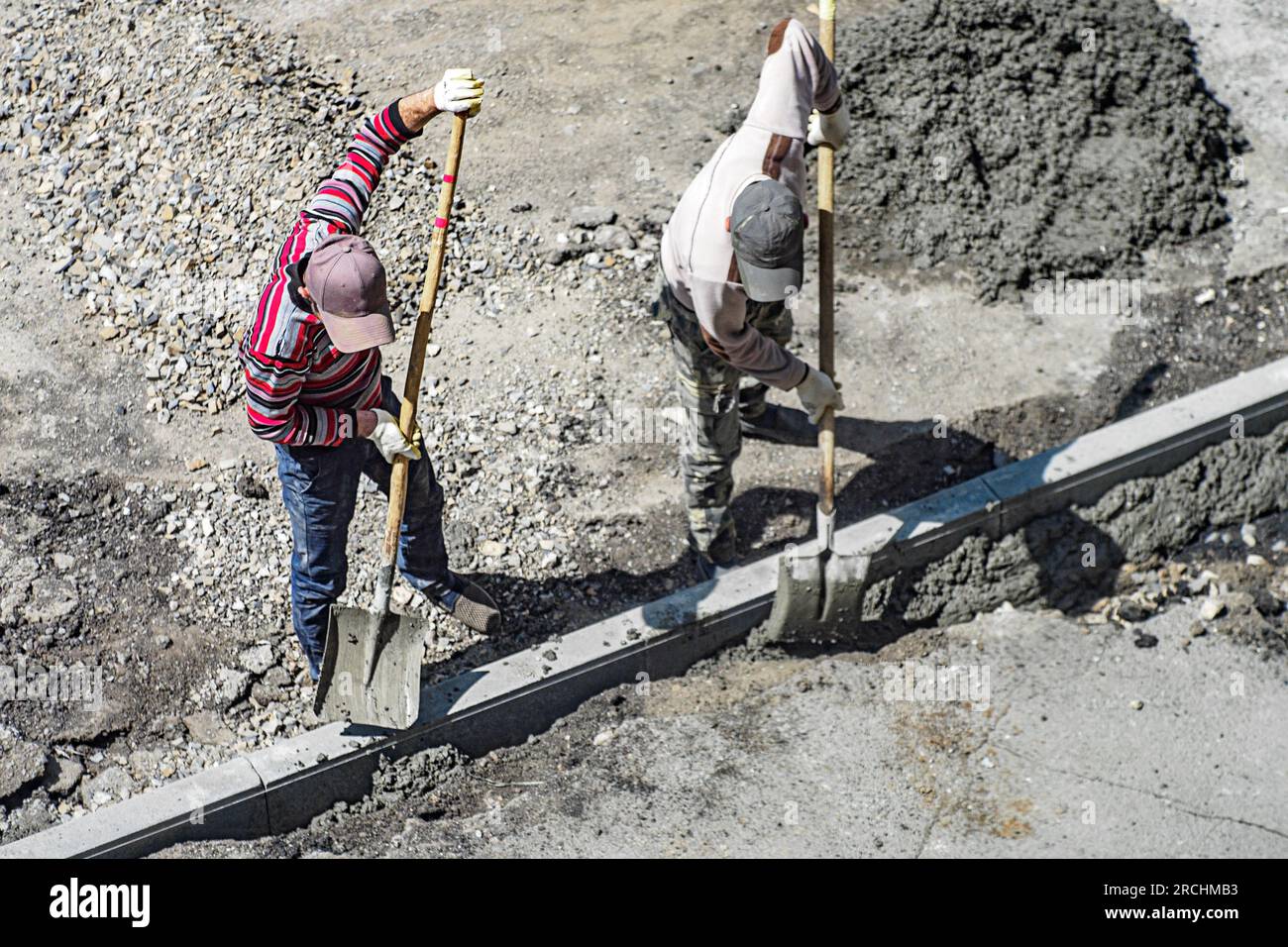 Roadway repair. Two handymen laying curbs on road on summer day ...