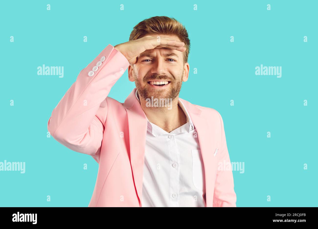 Happy young man in pink suit holds his hand on forehead above eyes and ...