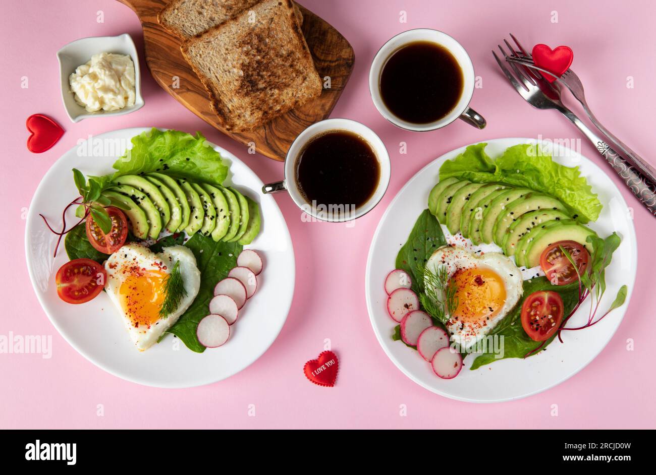 Romantic couple breakfast - two portions heart-shaped fried eggs with avocado, spinach, cherry ...