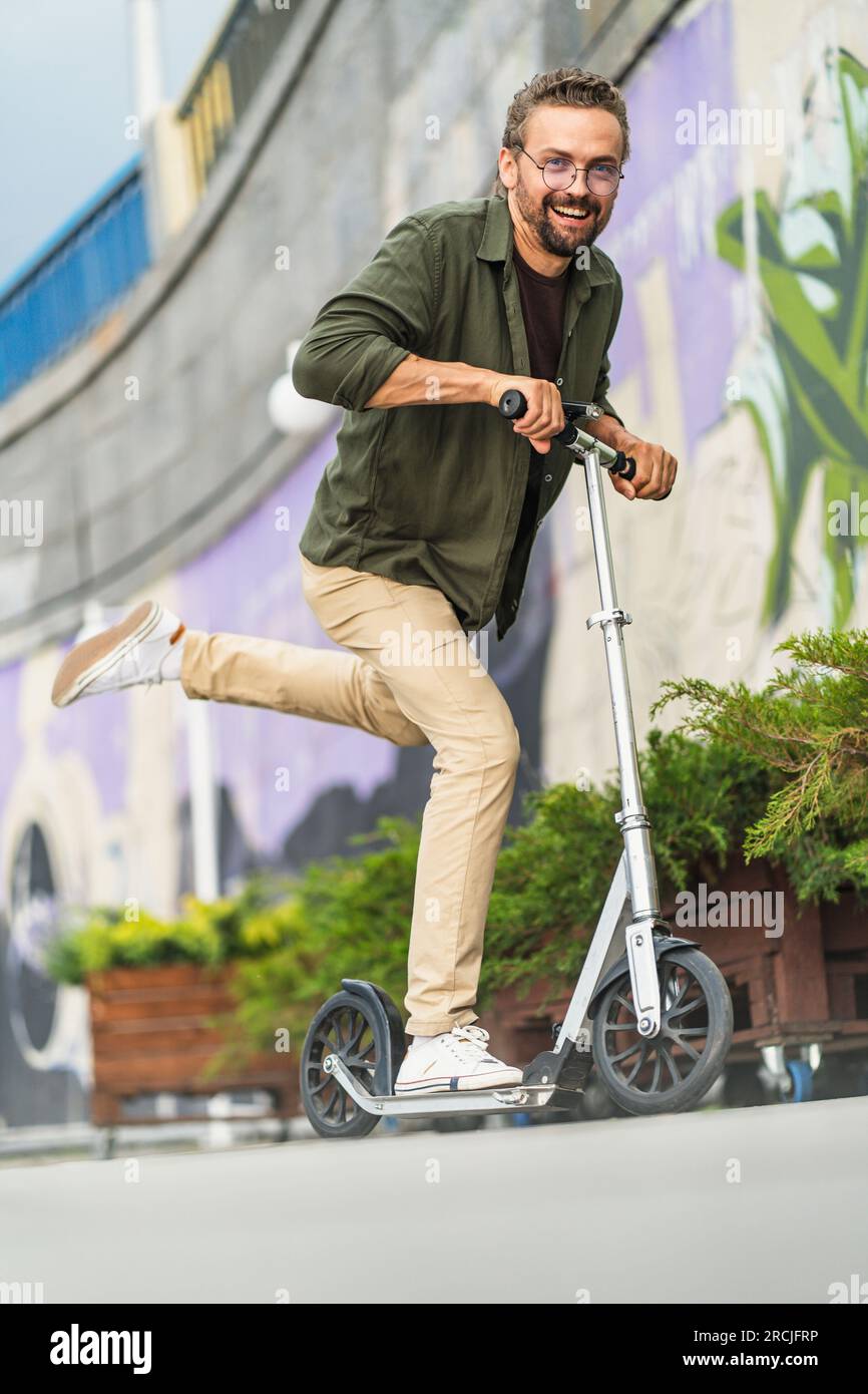 Happy and stylish metrosexual man riding a scooter on an urban ...