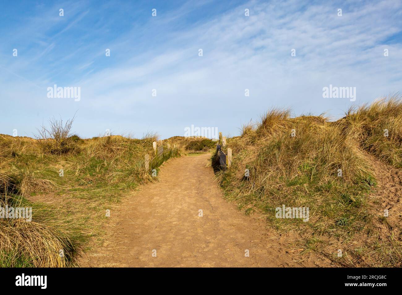 A sandy pathway through marram grass covered sand dunes, with a blue ...