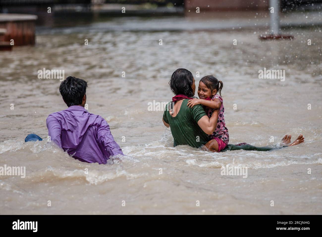 New Delhi, India. 14th July, 2023. People wades through a flooded road after a rise in the water ...
