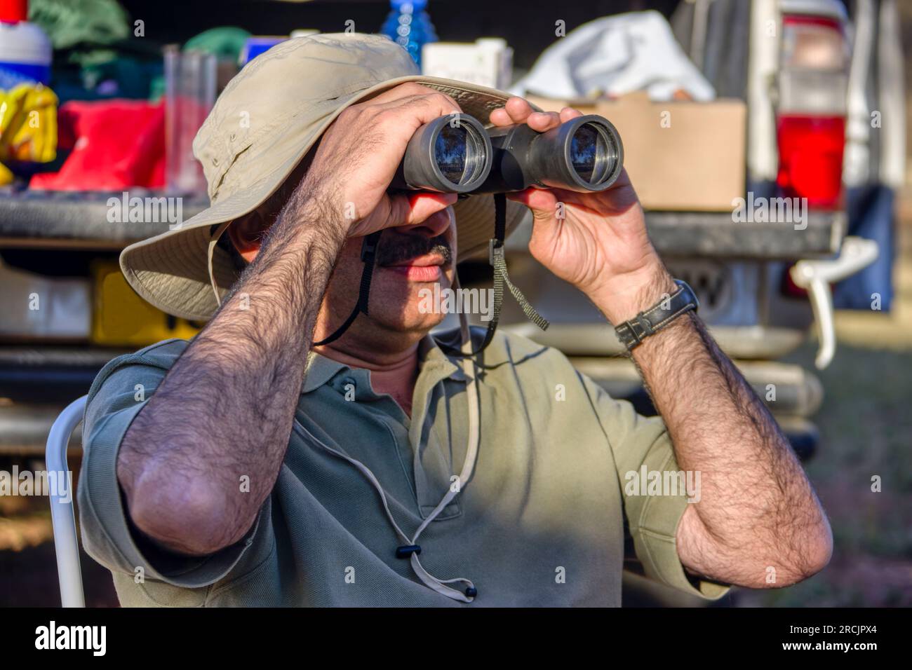 arab man with his binoculars and safari hat sited on a chair in front ...