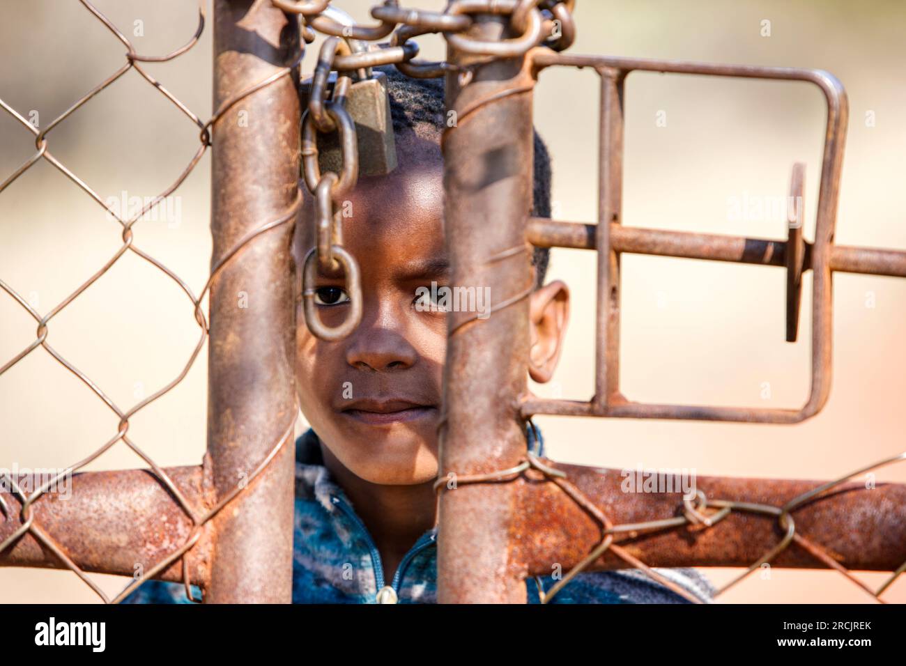 village african child with a no hope look locked behind a rusty metal ...