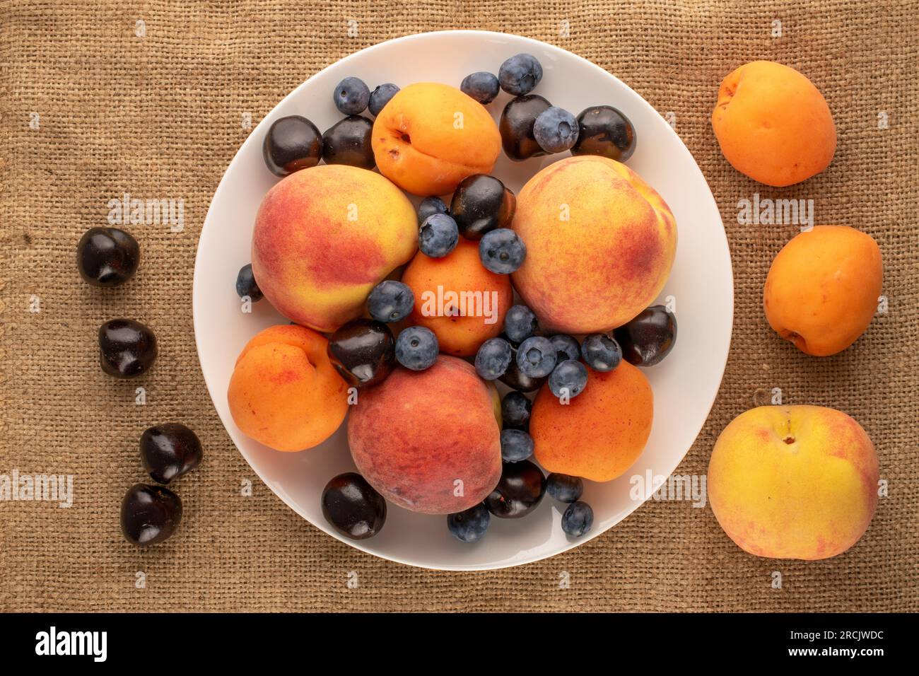 Fresh sweet fruits in white ceramic plate on jute cloth, macro, top ...