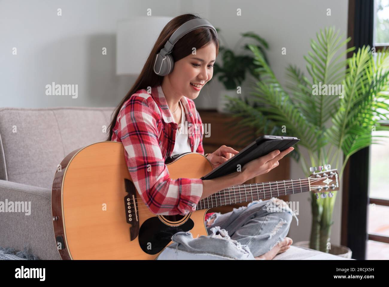 Guitar and singer concept, Young woman wear earphone and sit on couch ...