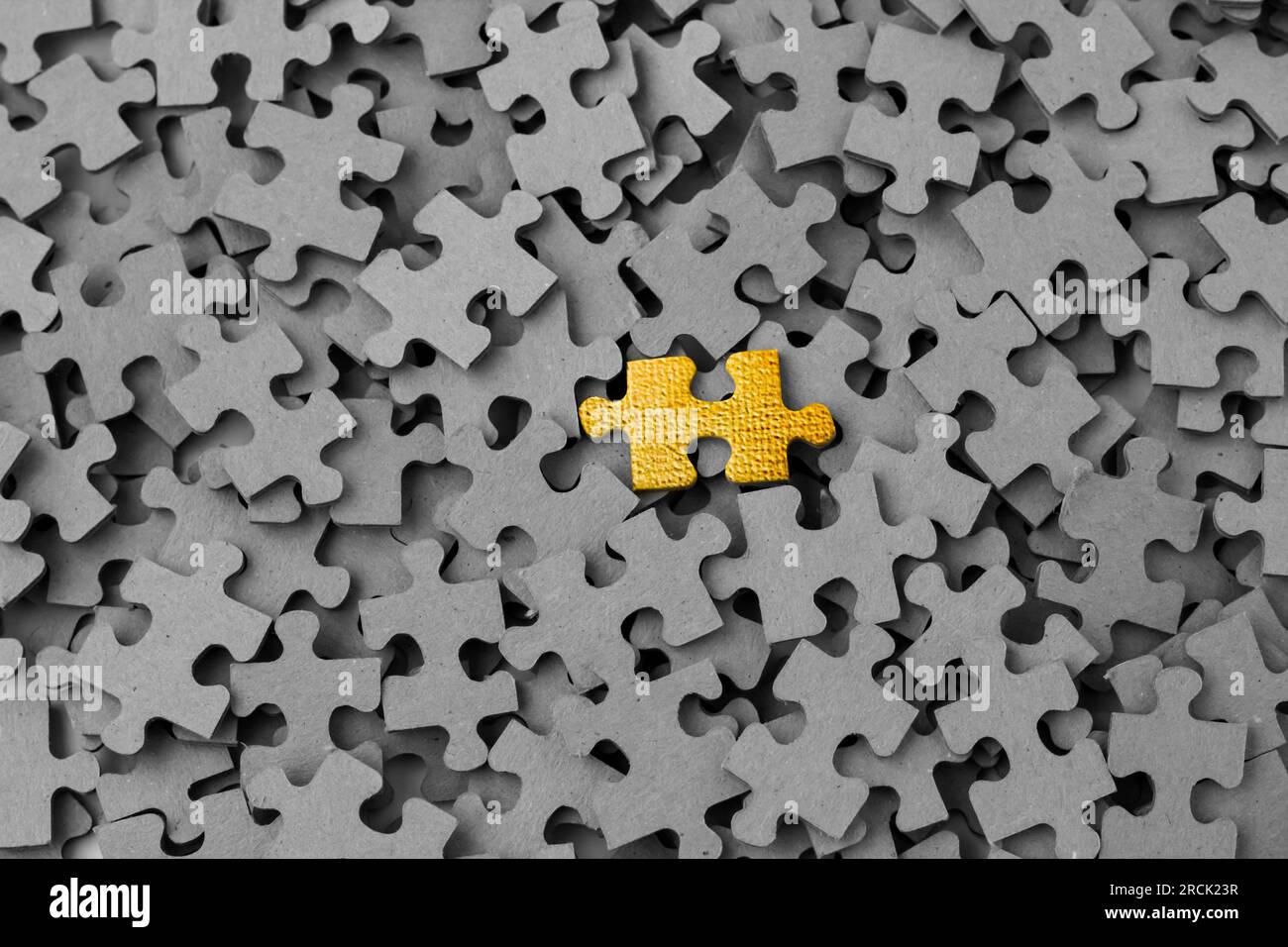 A yellow puzzle piece on top of many cardboard puzzle pieces with the ...