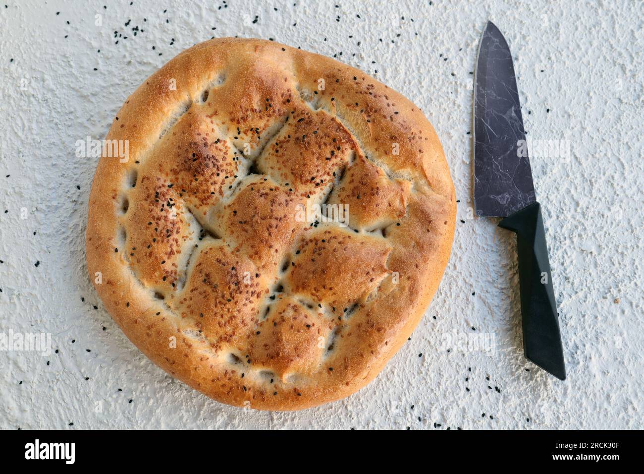 Traditional Turkish Ramadan Bread with a knife on a white textured ...