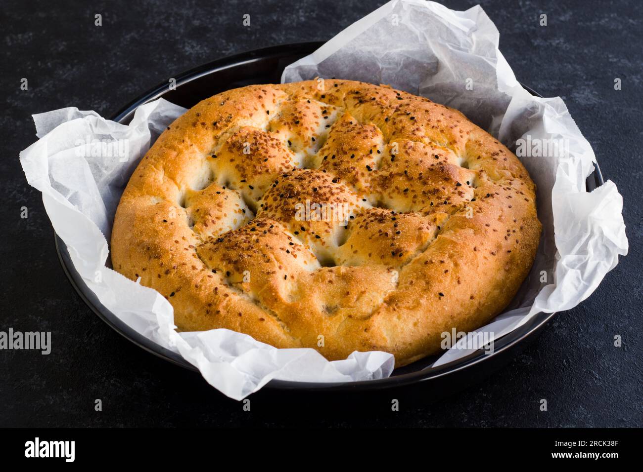 Traditional Turkish Ramadan Bread in baking tray on black surface with ...