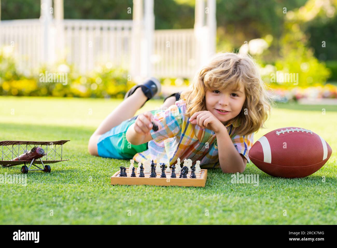 Child playing chess game in spring backyard, laying on grass ...