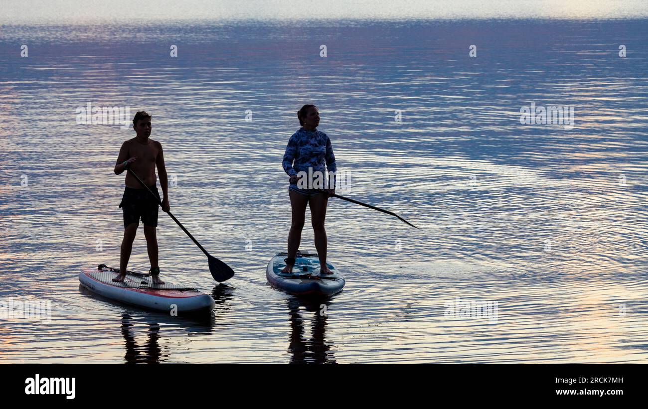 Woman and young boy on paddle board at sunset in the lake. Golden Lake ...