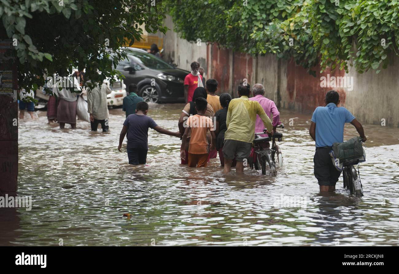 New Delhi, India. 15th July, 2023. People walk on a submerged street filled with water from ...