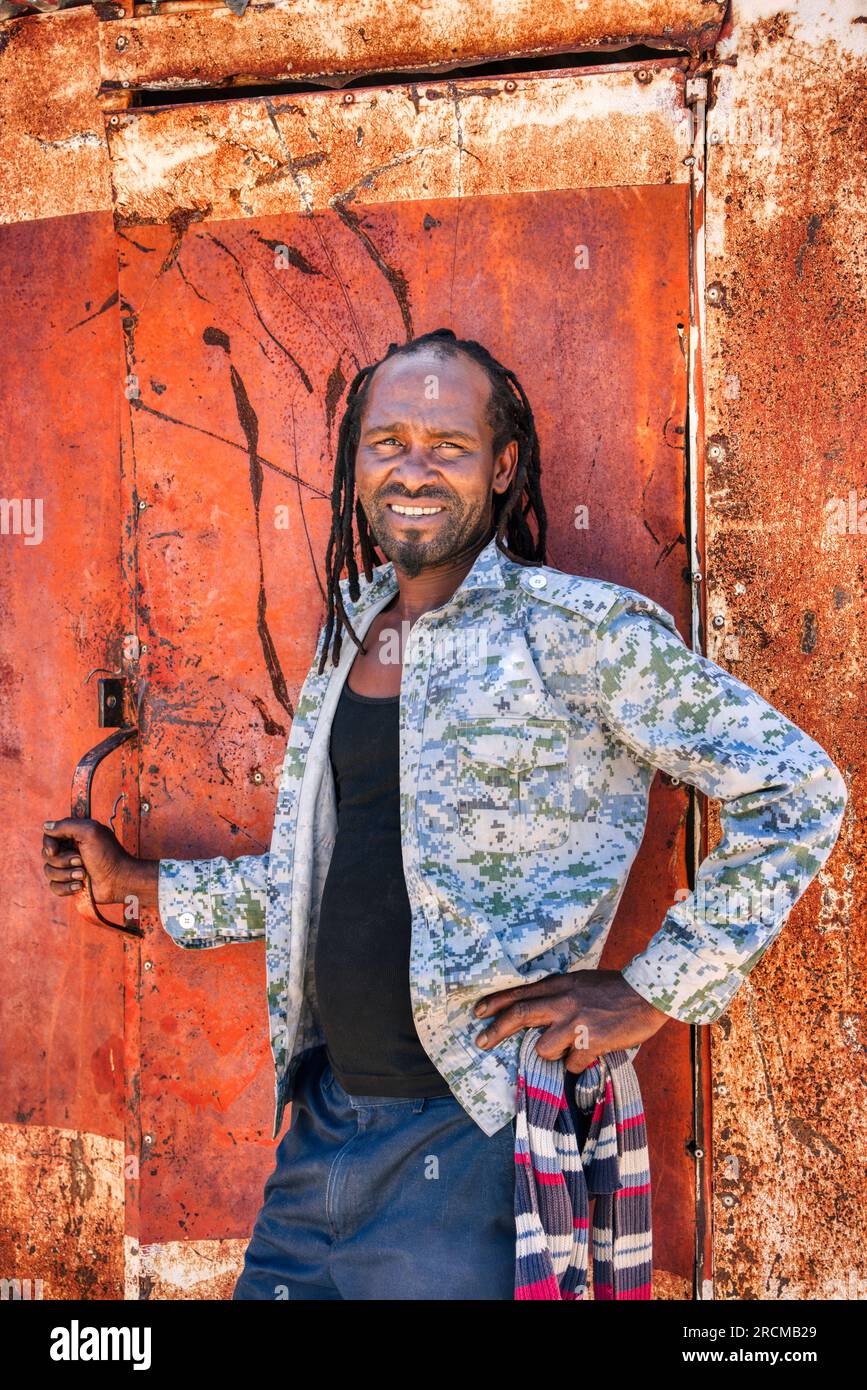 village young african Rastafarian man in front of the rusty metal shack ...