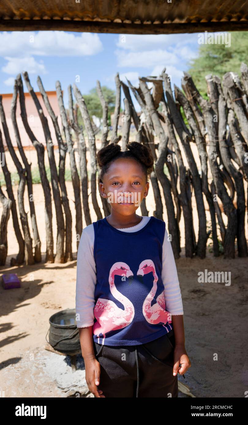 African village child standing under the shade in the shack, outdoors ...