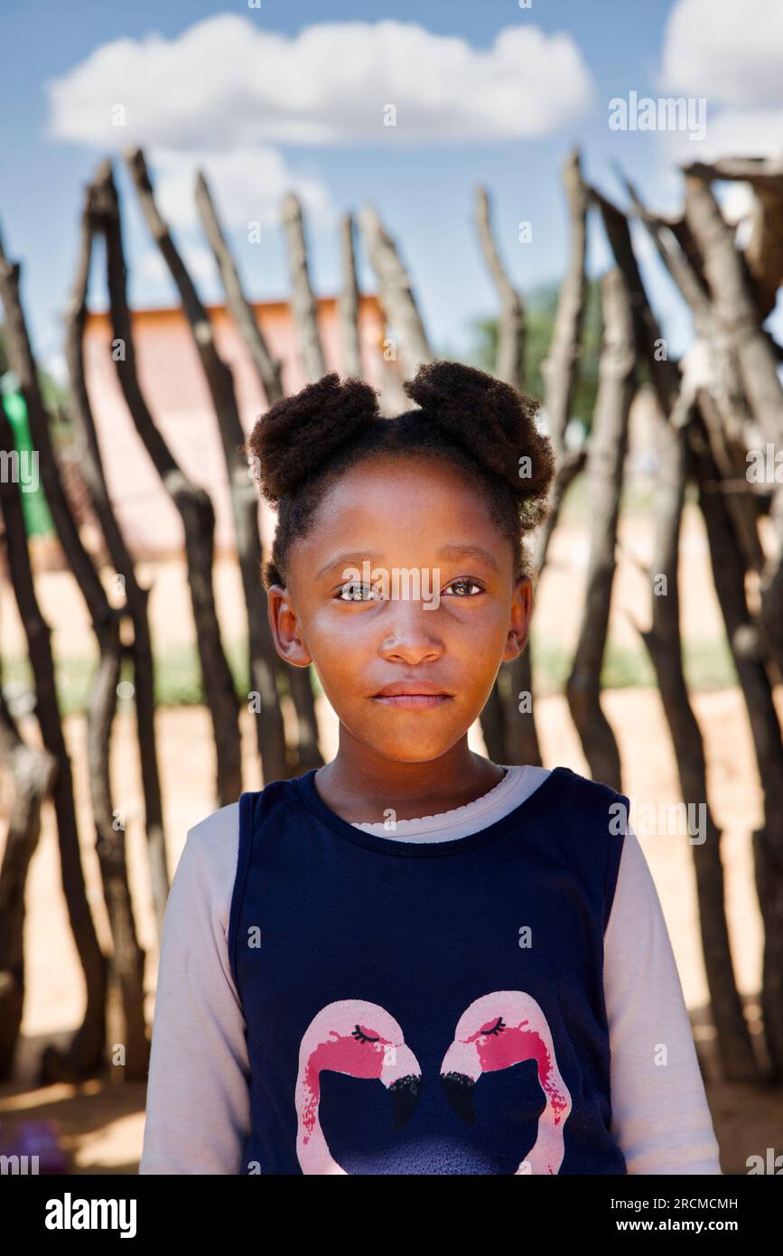 African village child standing under the shade in the shack, outdoors ...