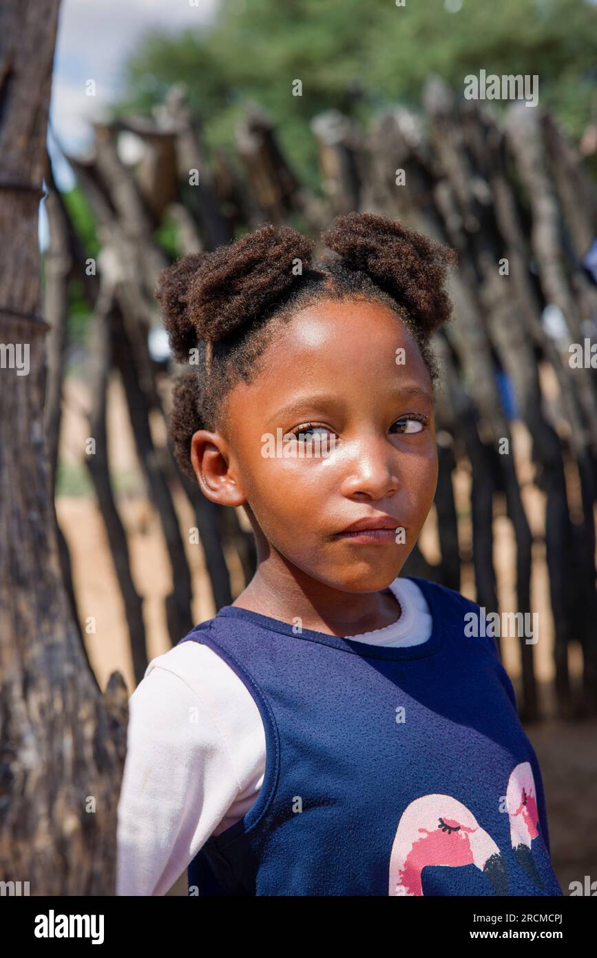 African village child standing under the shade in the shack, outdoors ...