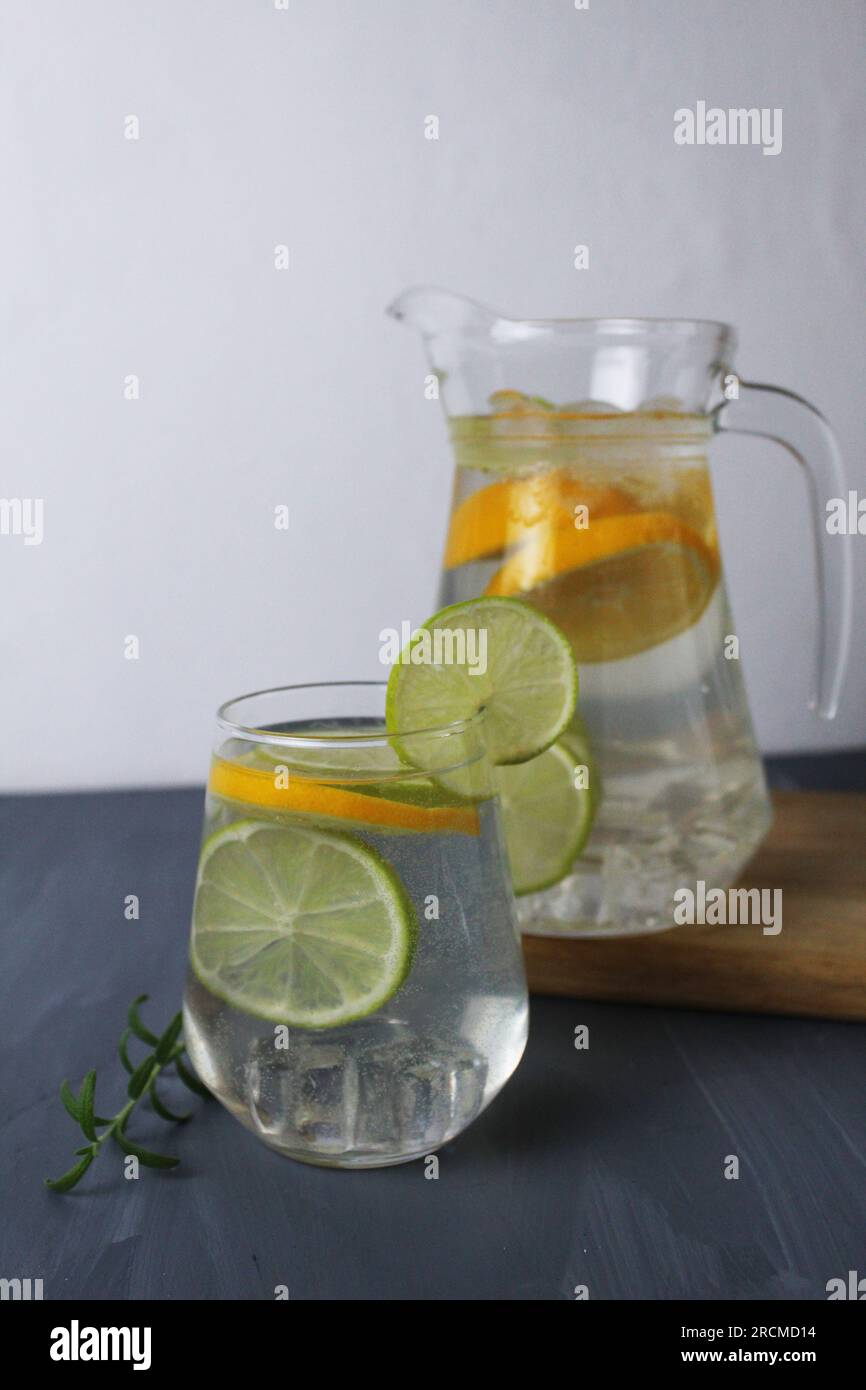 Citrus lemonade in a glass jug and a glass, lemon, orange, lime lie on ...