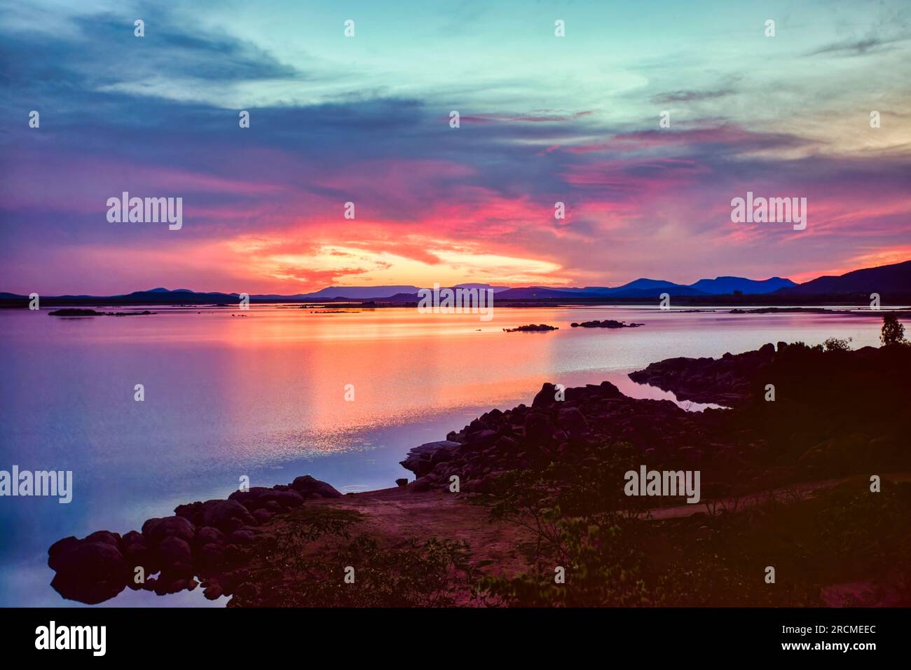 lake shore at sunset with an orange violet sky and sun setting down ...