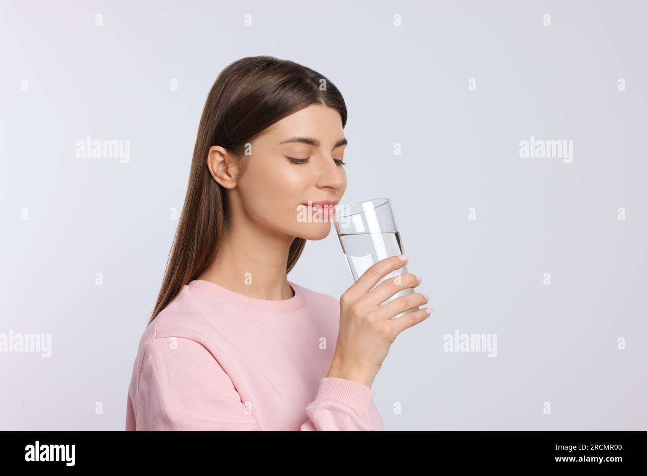 Healthy habit. Woman drinking fresh water from glass on light grey ...
