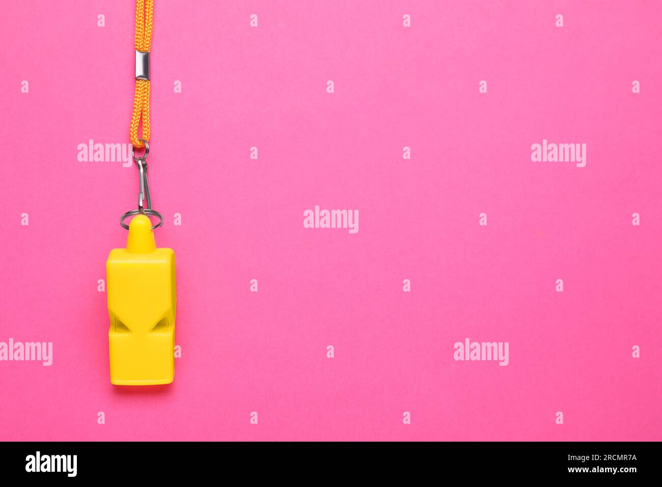One yellow whistle with cord on pink background, top view. Space for ...
