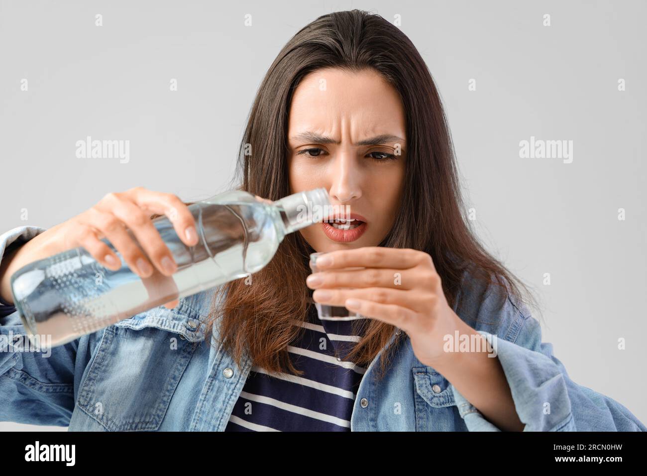 Drunk young woman pouring vodka into glass on light background Stock ...