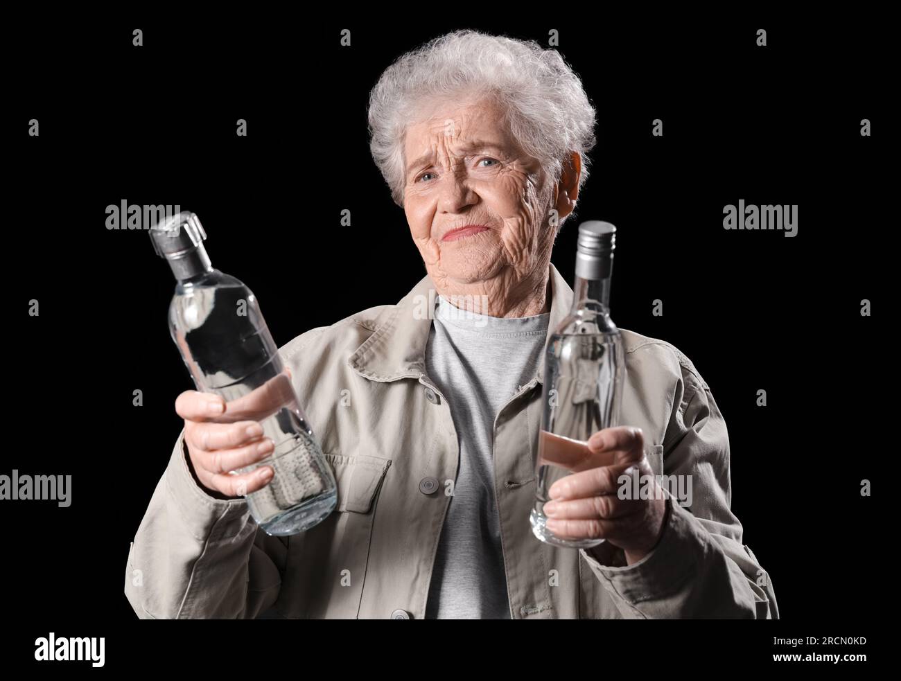 Displeased senior woman with bottles of vodka on black background Stock ...