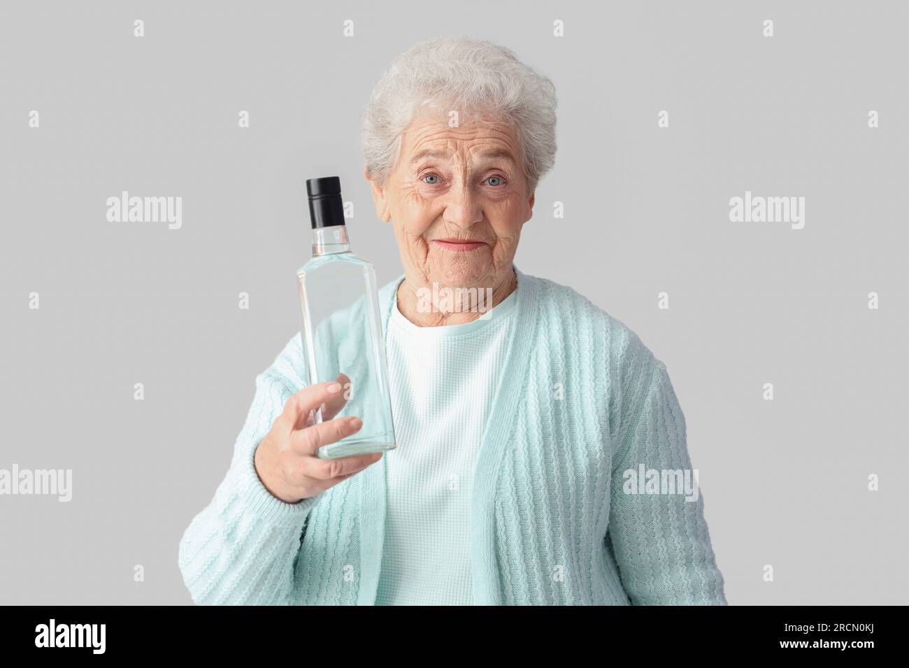 Senior woman with bottle of vodka on light background Stock Photo - Alamy