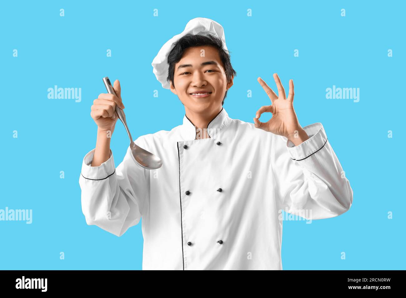 Male Asian chef with ladle showing OK on blue background Stock Photo ...